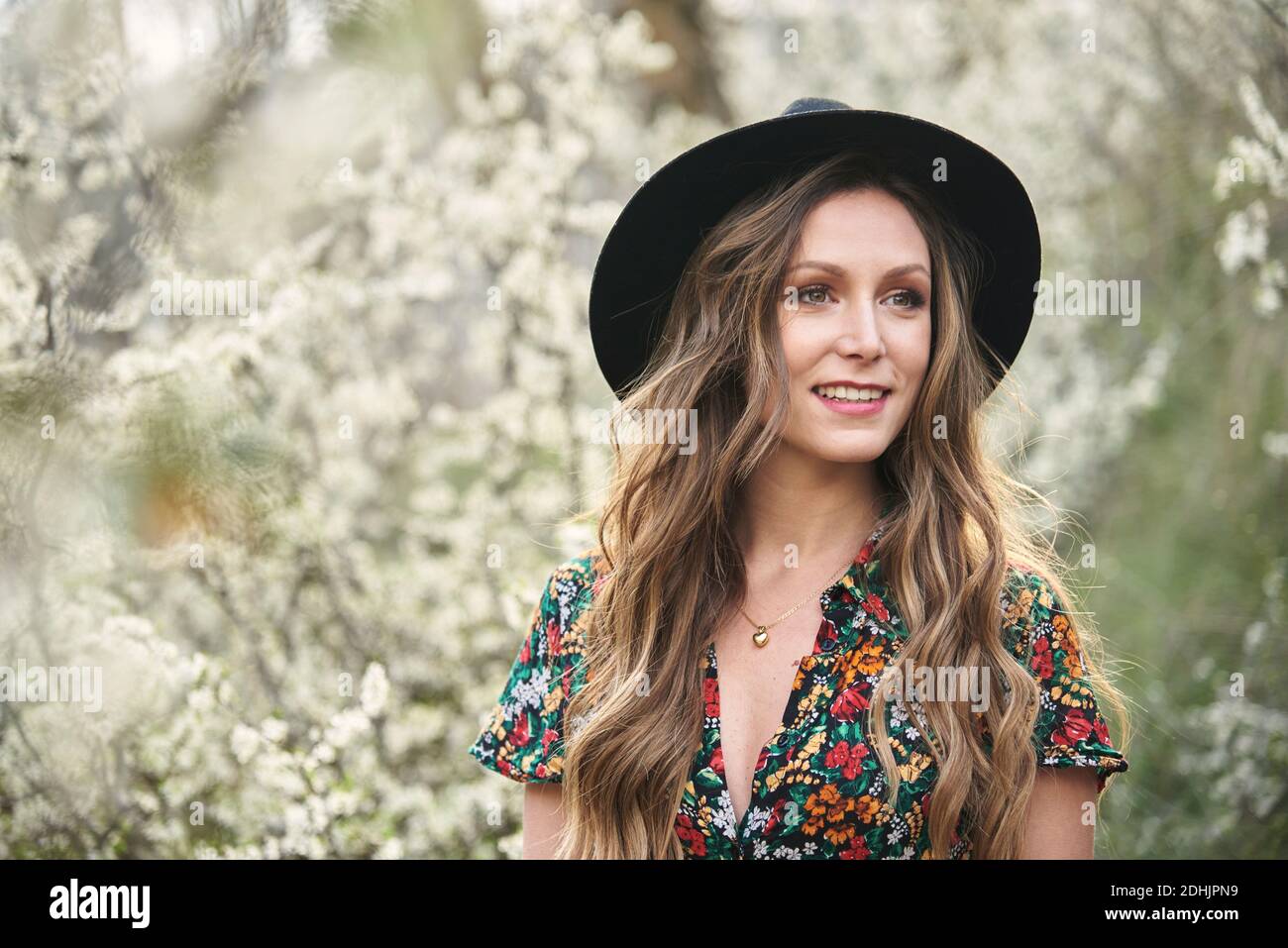 Gentle female in long dress walking in spring park among blooming trees ...