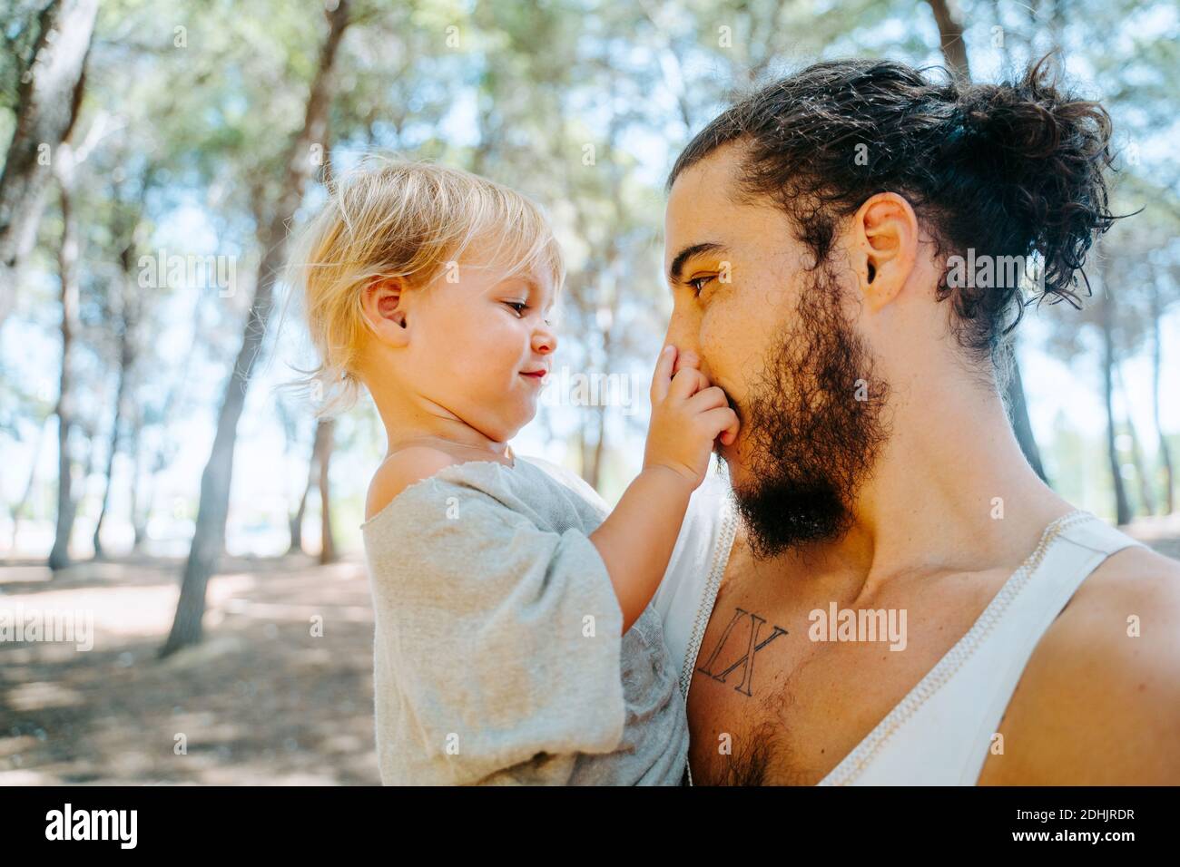 Side view of loving ethnic father gently cuddling cute child in cheek ...