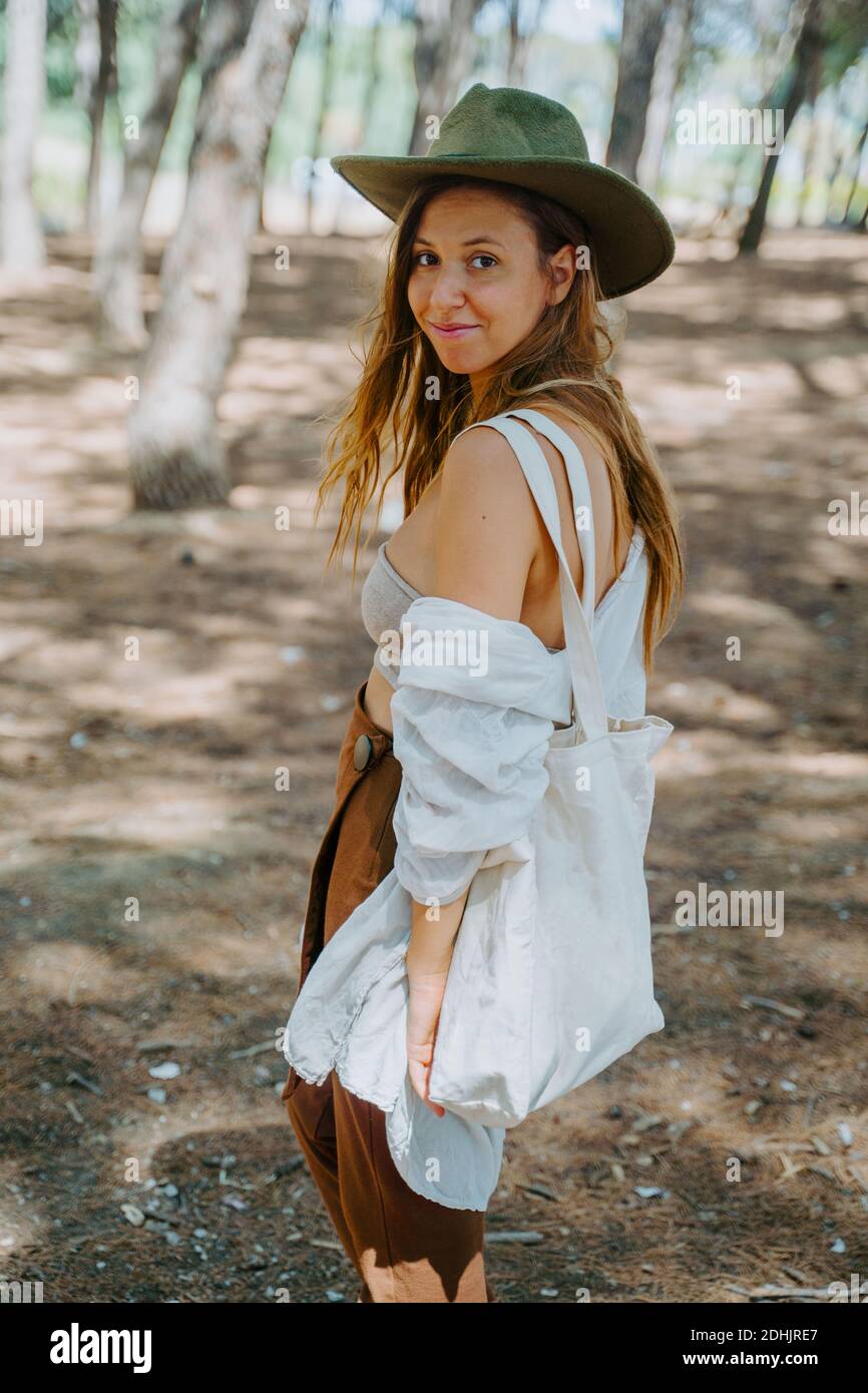 Happy female hippie in hat and top standing in woods and enjoying ...