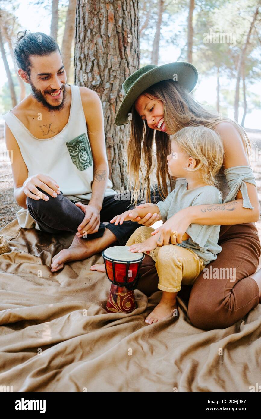 Delighted mother and father teaching little kid playing bongo drum ...
