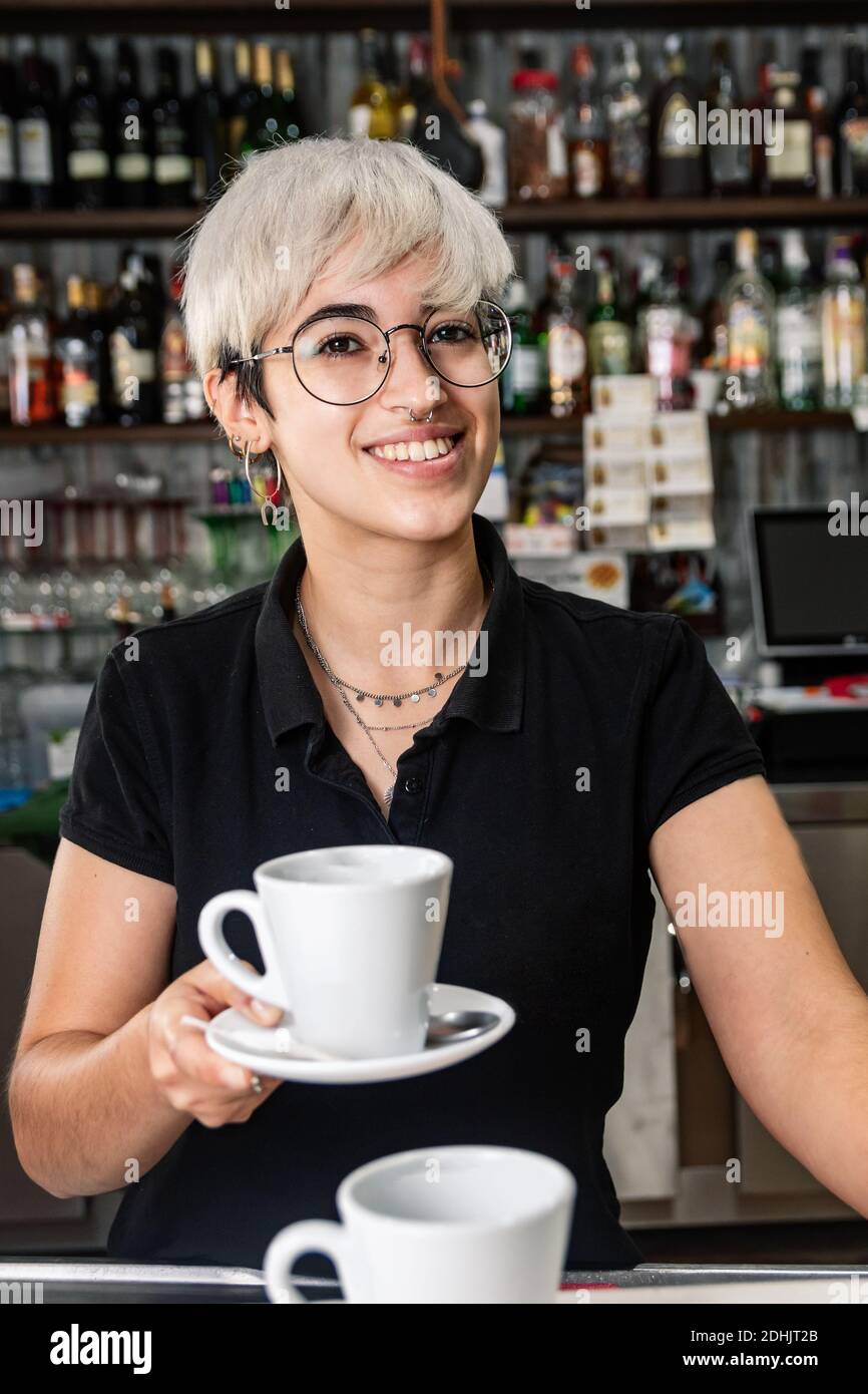 Cheerful female bartender standing at counter with cup of freshly ...