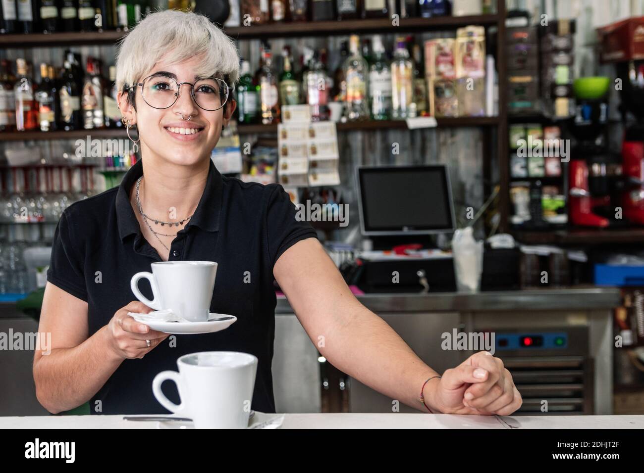 Cheerful female bartender standing at counter with cup of freshly ...