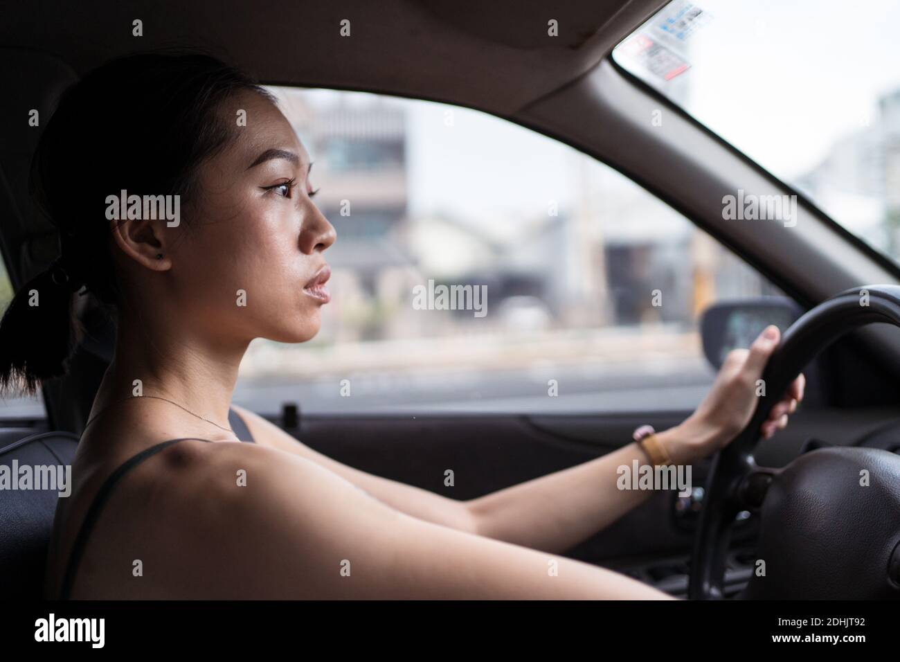 Side view of focused Asian female driving modern automobile along road ...