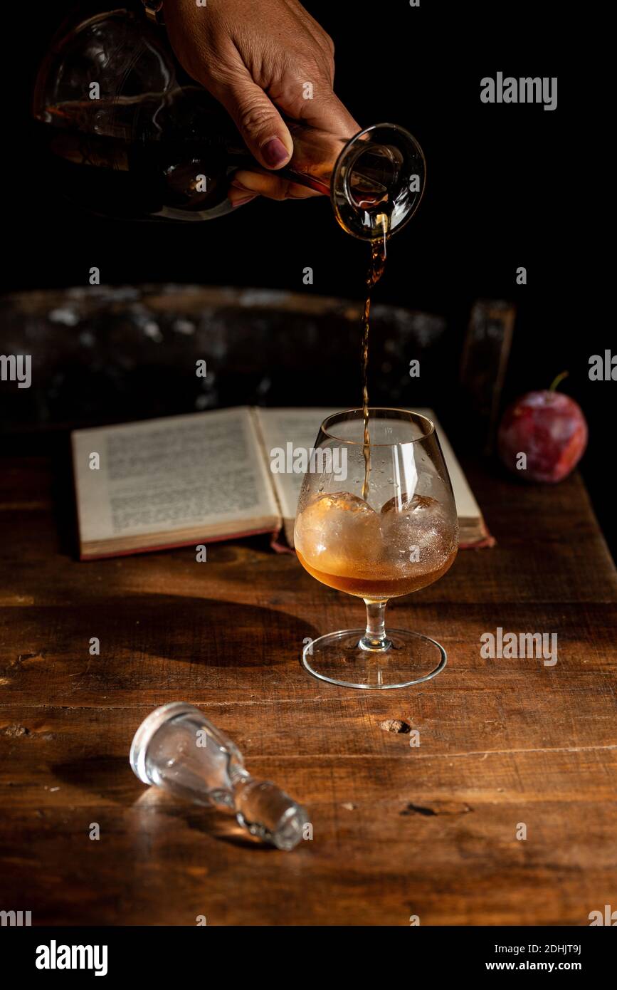 Crop anonymous person pouring cognac from decanter into glass placed on ...