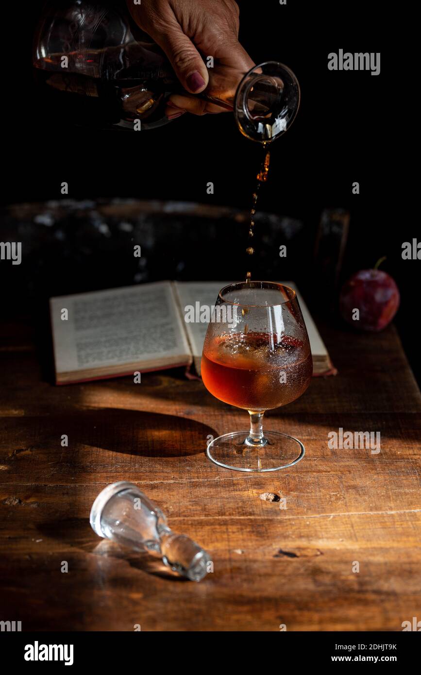 Crop anonymous person pouring cognac from decanter into glass placed on ...