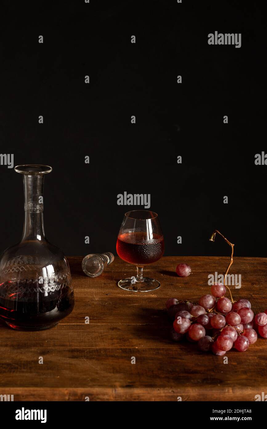Still life composition with glass and decanter with cognac placed near bunch of red grapes on ...