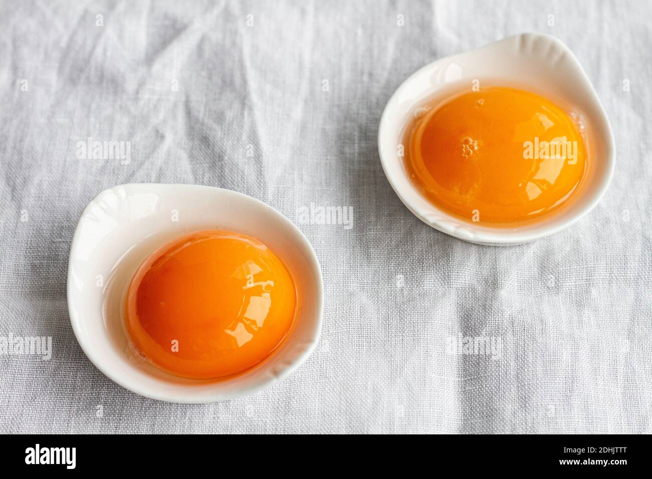 High angle of small white bowls with uncooked egg yolks placed on white ...