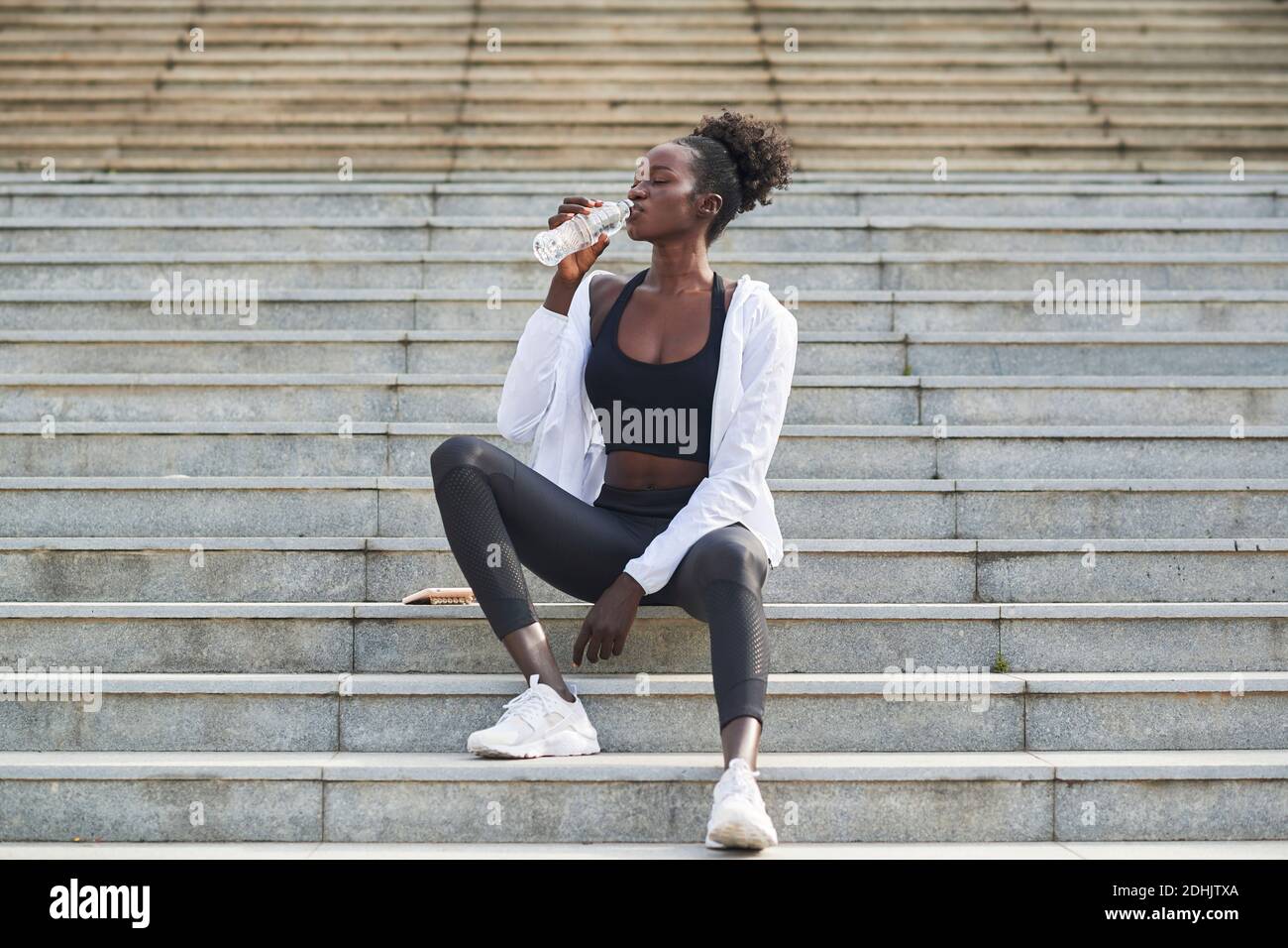 Relaxed African American female runner sitting on stairs in city and ...