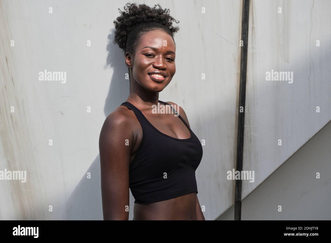 Cheerful African American female athlete wearing sports bra leaning on ...