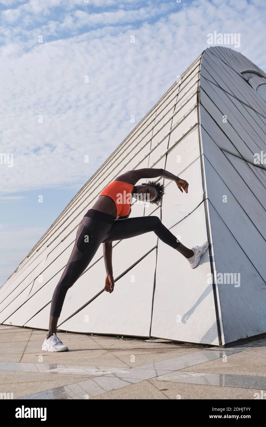 Low angle side view of flexible African American female runner warming ...