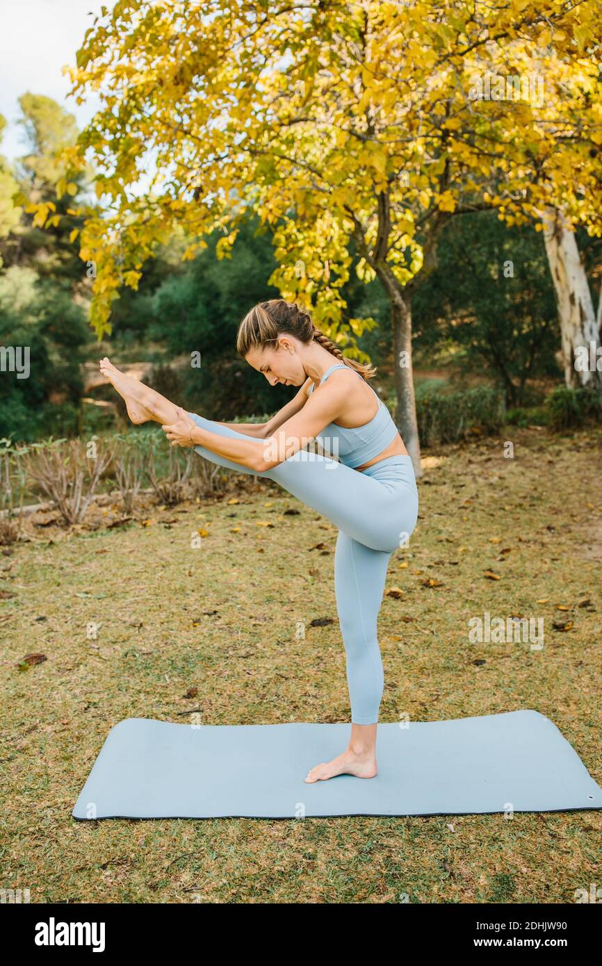 Full body side view of focused young slim female standing on one leg ...