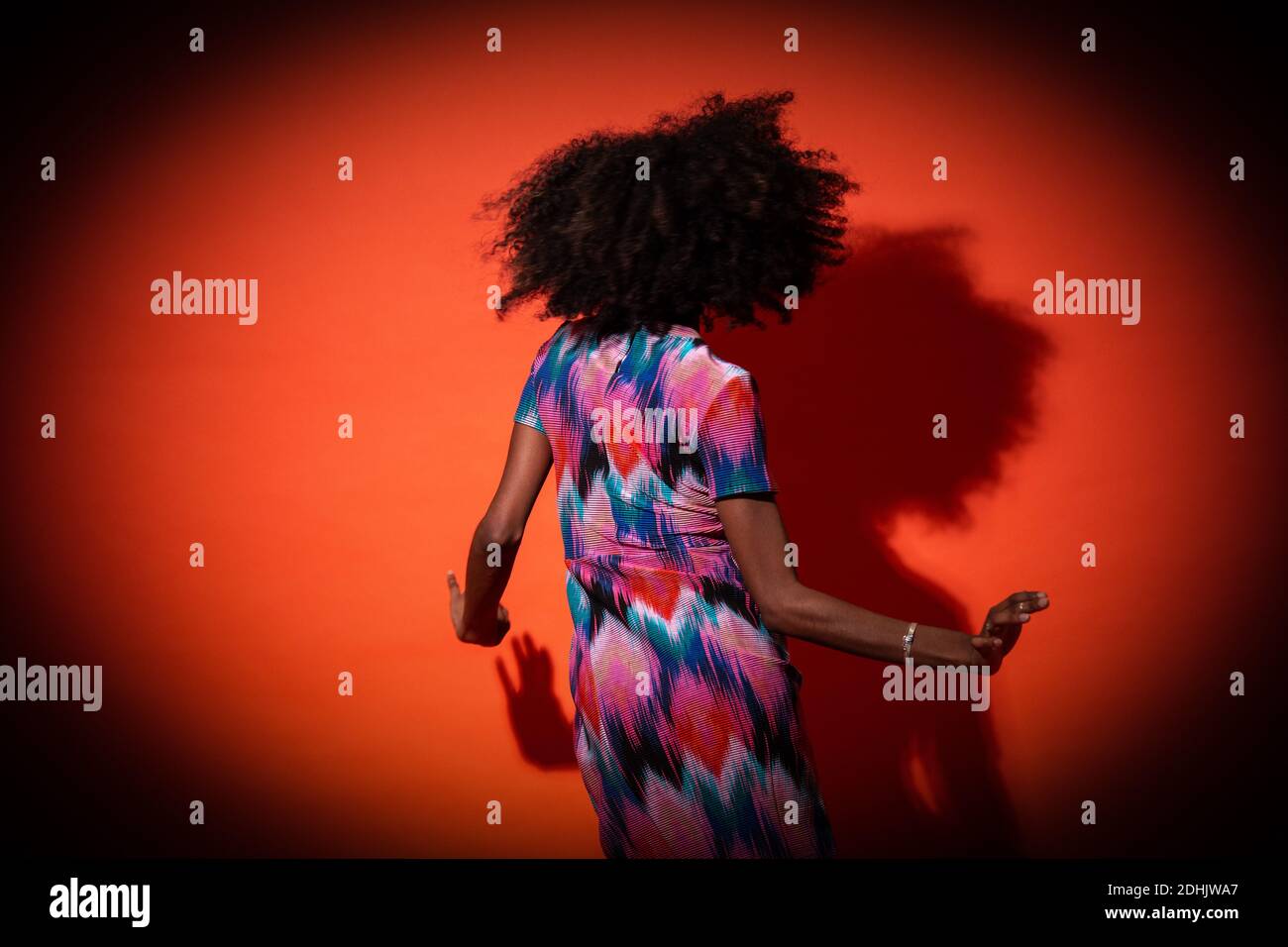 Back view black Woman with Afro hairstyle wearing vivid dress against ...