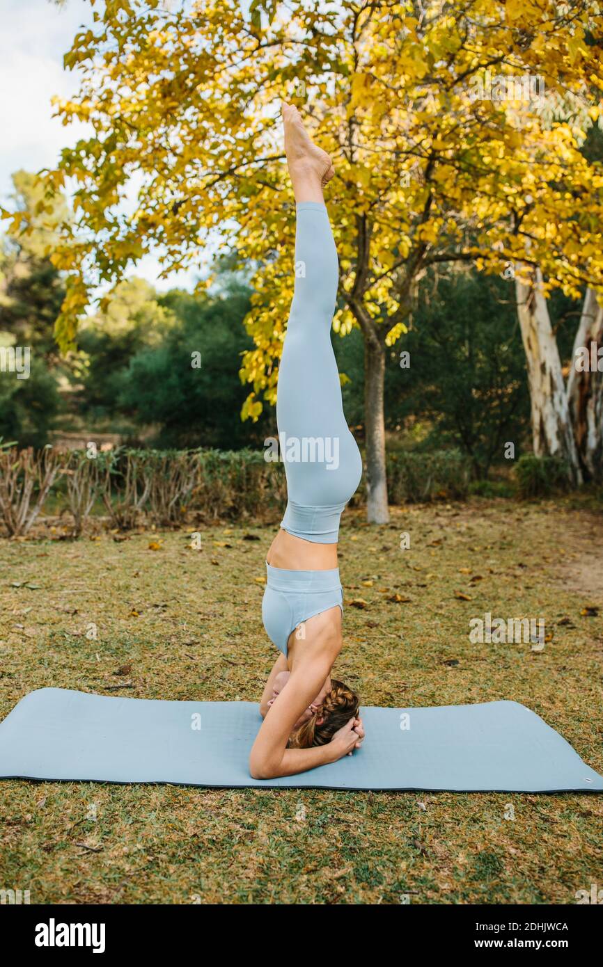 Side view of slender female balancing in Salamba Sirsasana on mat while ...