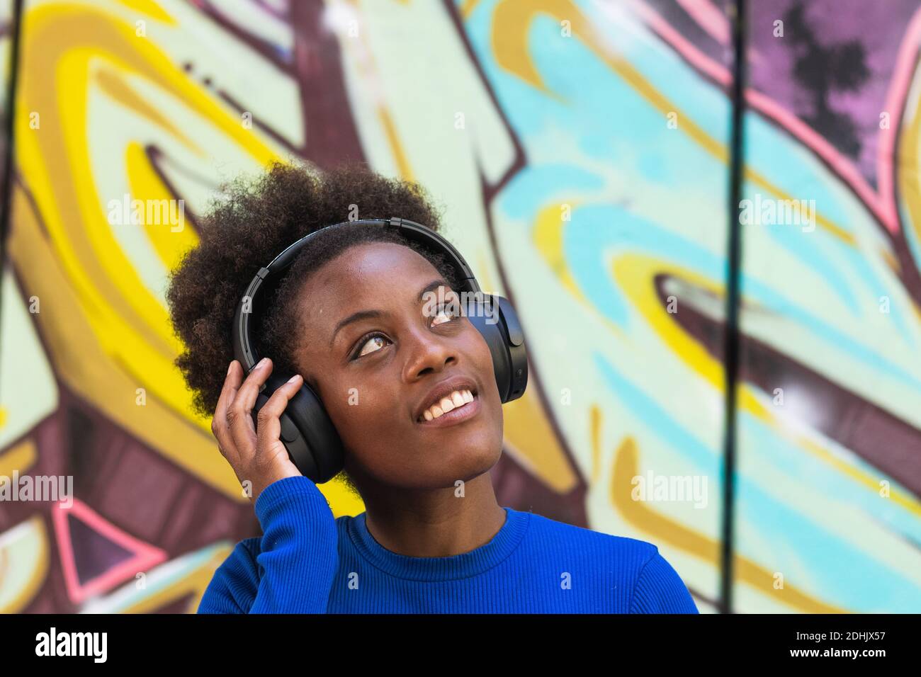 Optimistic black female with Afro hairstyle listening to music in ...