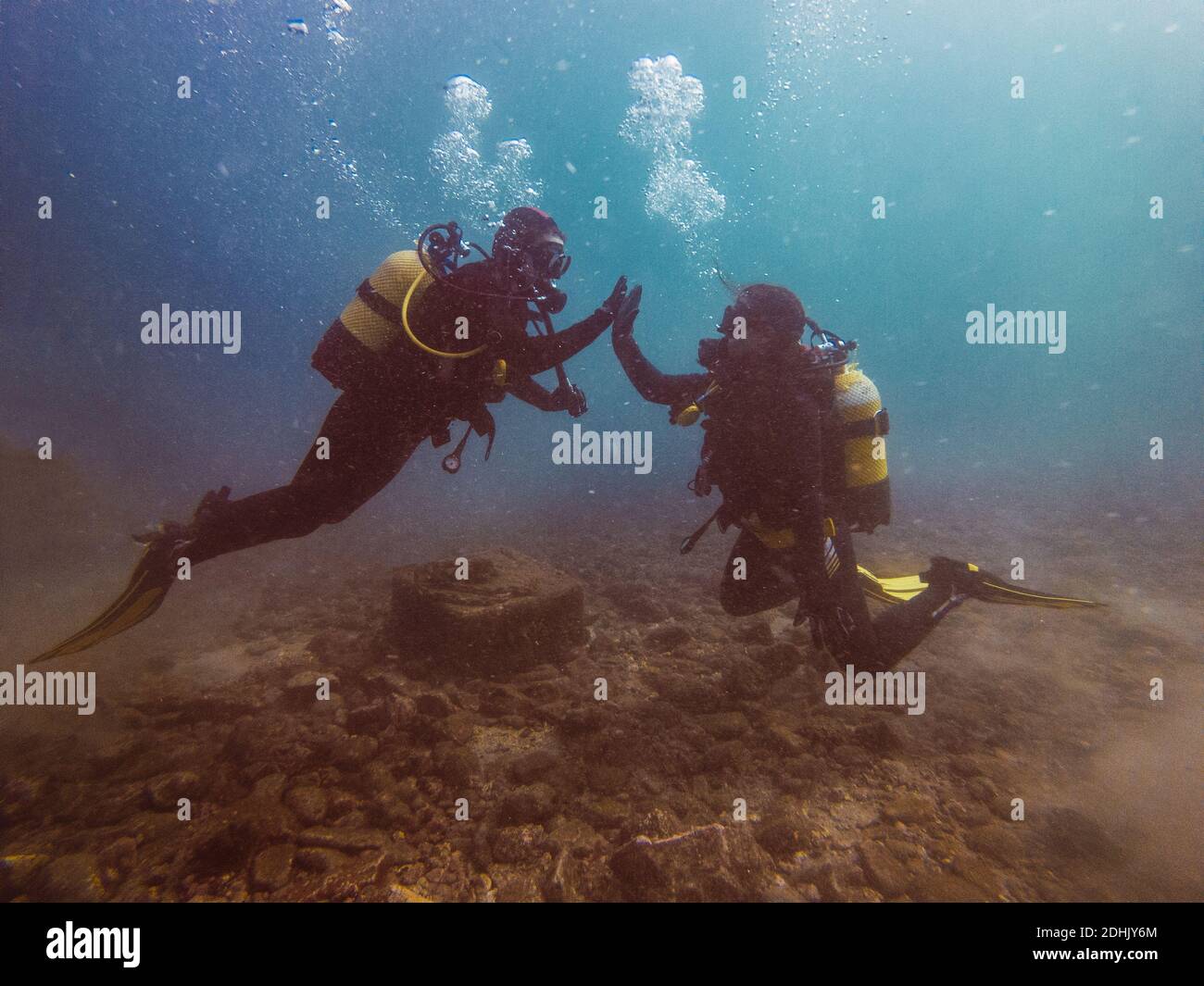 Side view unrecognizable divers giving high five together on the bottom ...