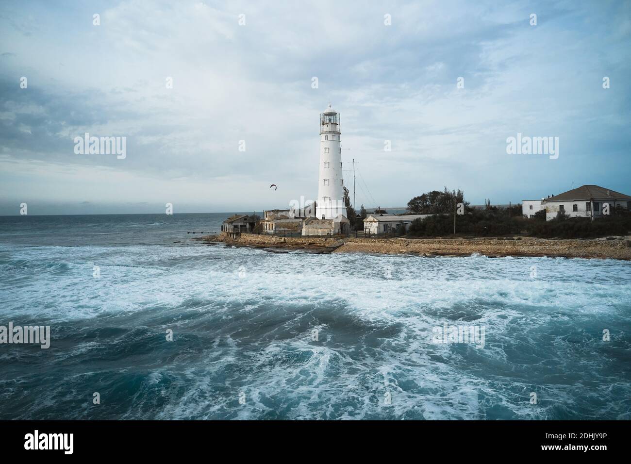 White lighthouse tower and small settlement located on rocky coast ...