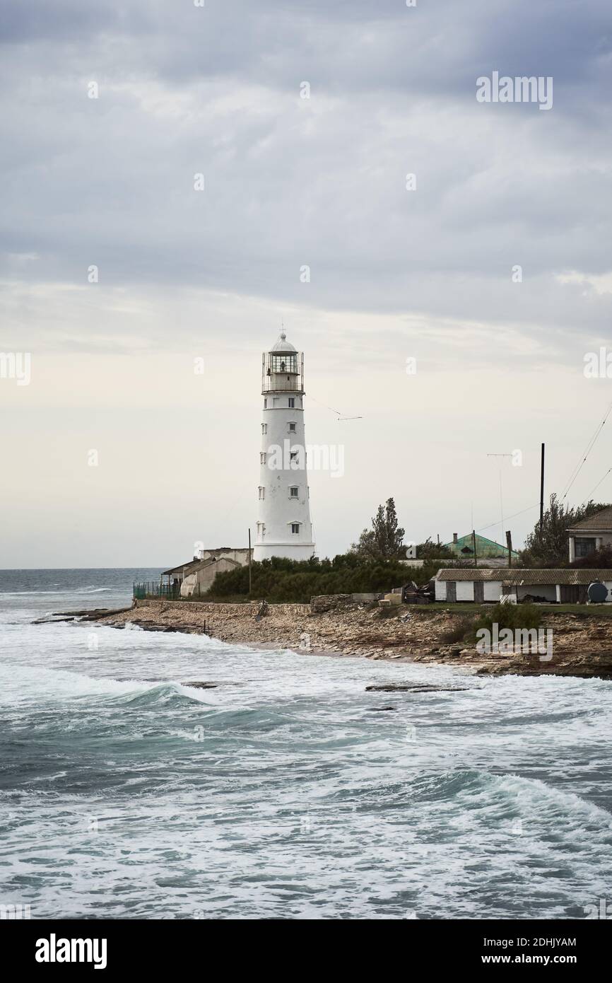 Tower of white beacon located on coast near waving sea under overcast ...