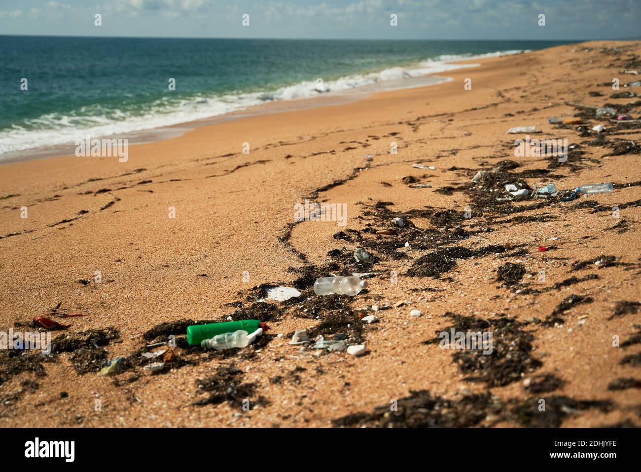 Sandy shoreline with trash and garbage scattered near blue sea on sunny ...