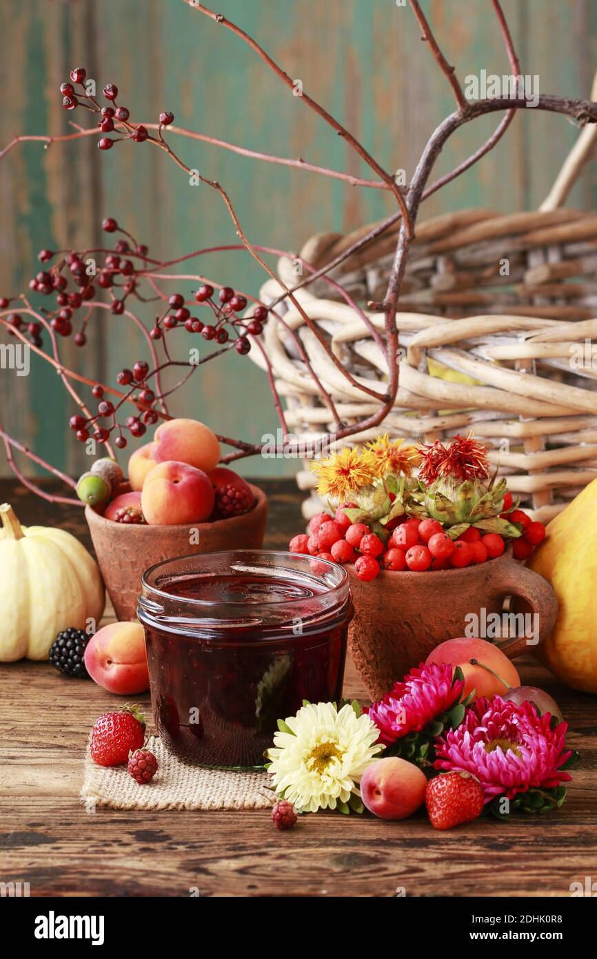 Dark jam in glass jar. Colorful autumn fruits and vegetables around ...