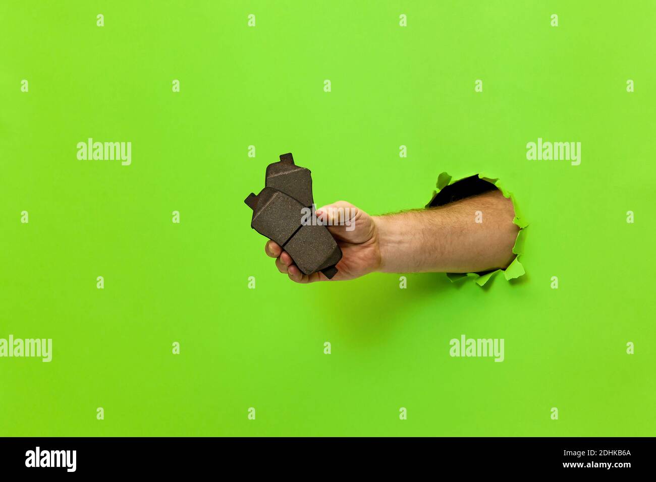 A man's hand holds car brake pads through torn green paper. Hand ...