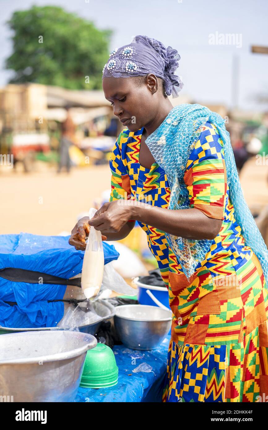 A view of an African lady standing in front of her stand at the outdoor ...