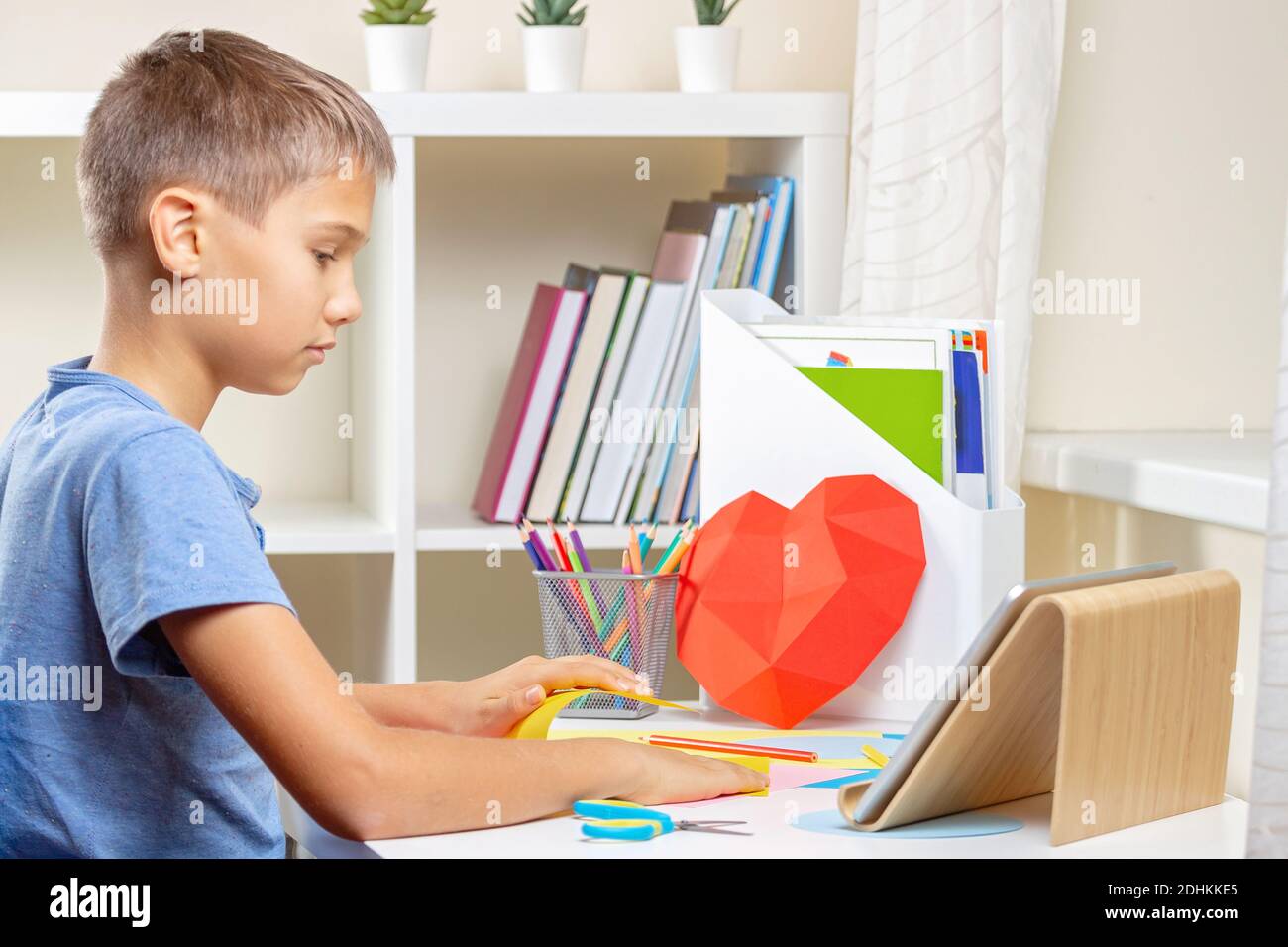 Boy watching video tutorial and making red polygonal paper heart ...