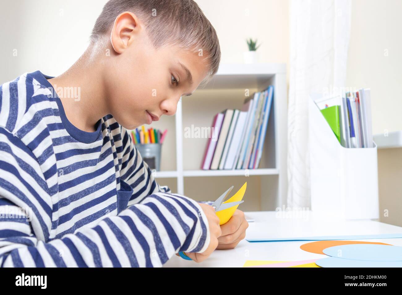 Boy cutting colored paper with scissors and making paper craft project ...