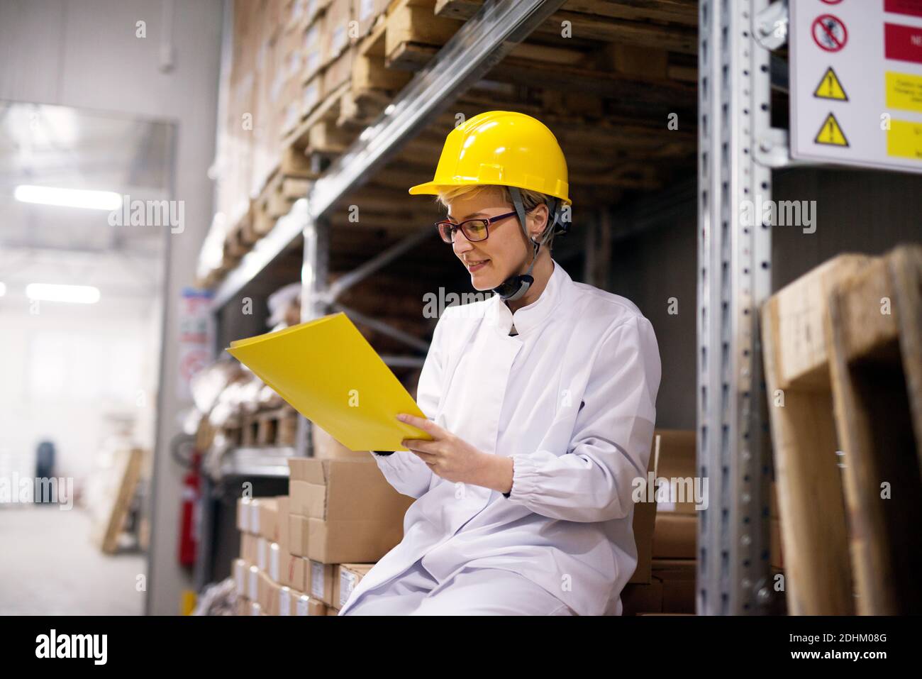 Young female dedicated engineer is sitting on stacks of boxes and ...