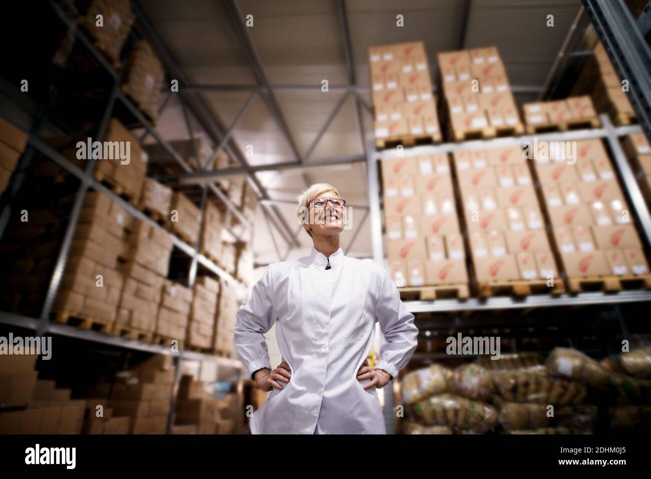 Young beautiful proud female worker is holding her arms on her hips and ...