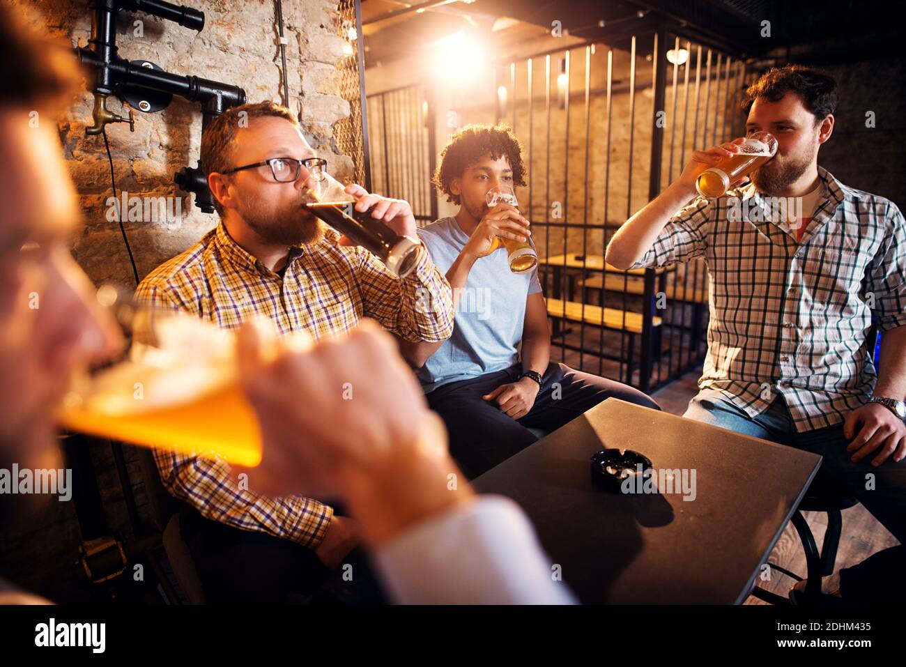 Four casual multicultural friends drinking beer while sitting in the ...