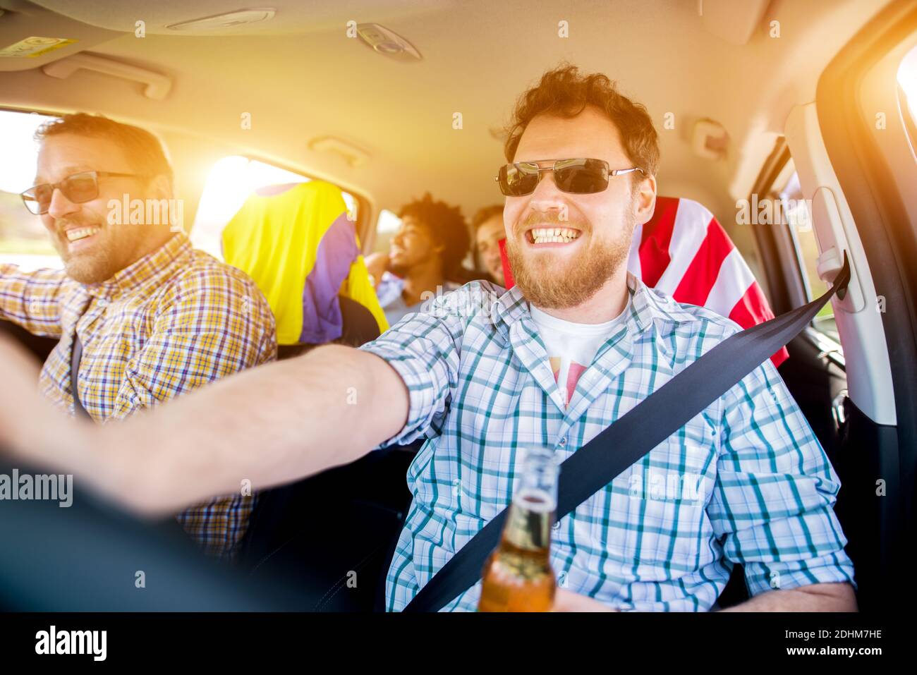 Portrait of joyful young man driving with beer and sunglasses while his ...