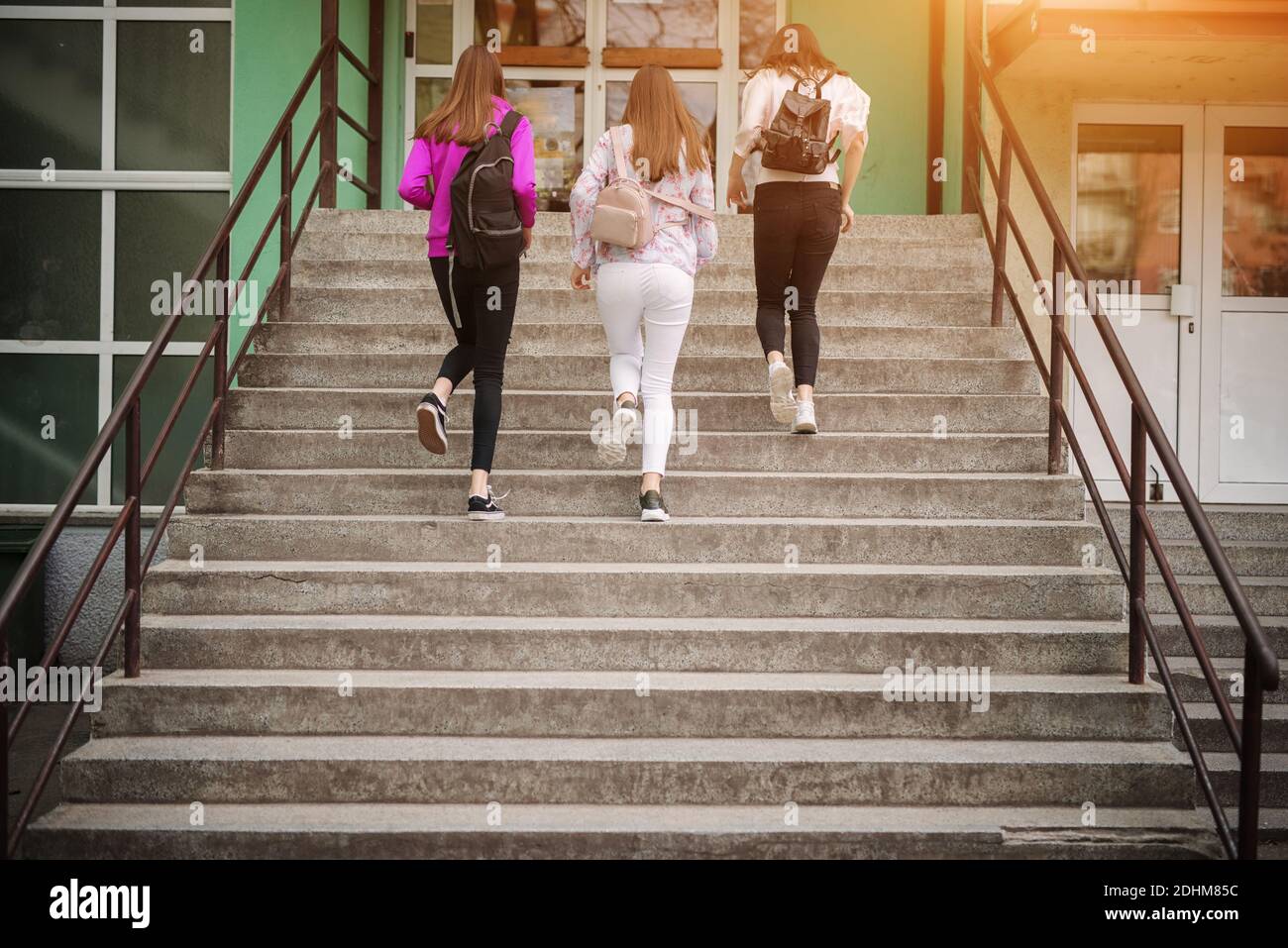 Rear view of three high school girls with backpacks running upstairs in ...