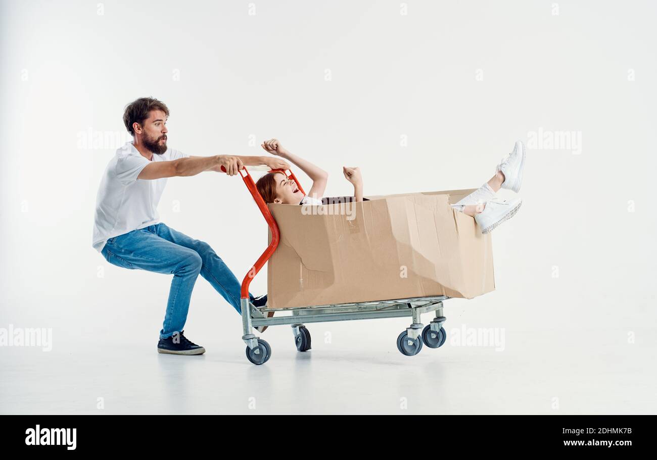 woman in a box on a cargo trolley and a cheerful male courier on a ...