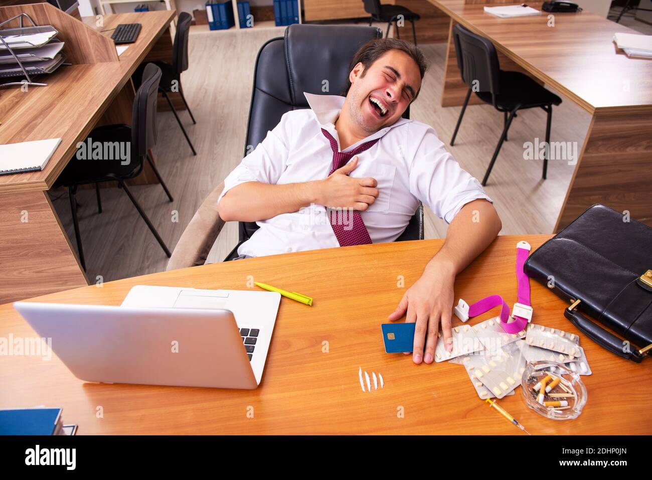 Young drug addicted male employee sitting at workplace Stock Photo - Alamy