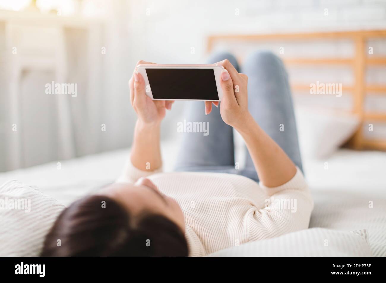 young woman watching the mobile phone screen and lying on the bed at ...