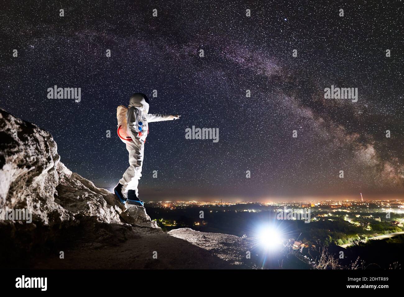 Space traveler pointing finger at night city while standing on rocky ...