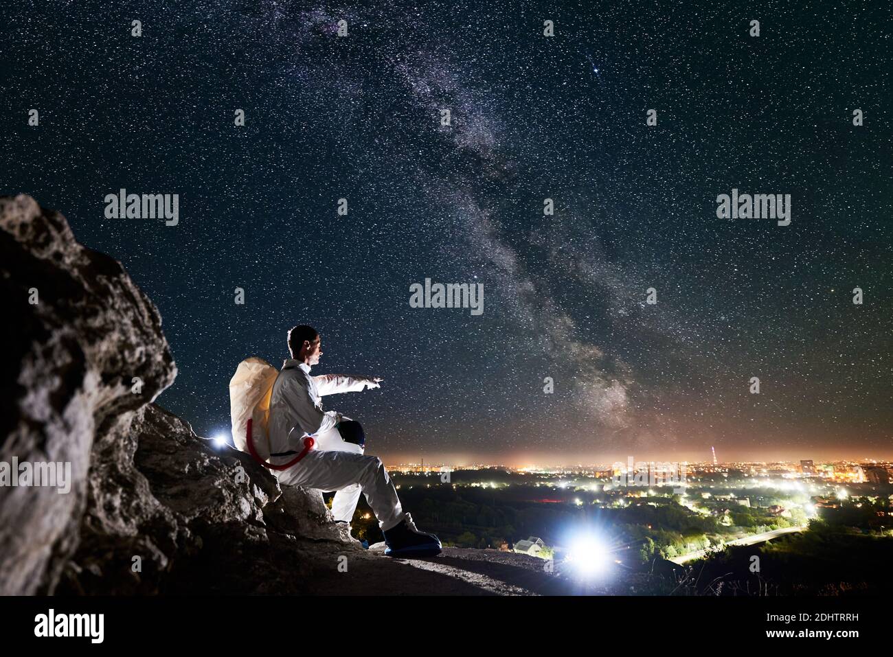 Side view of spaceman pointing finger at night city in valley while ...