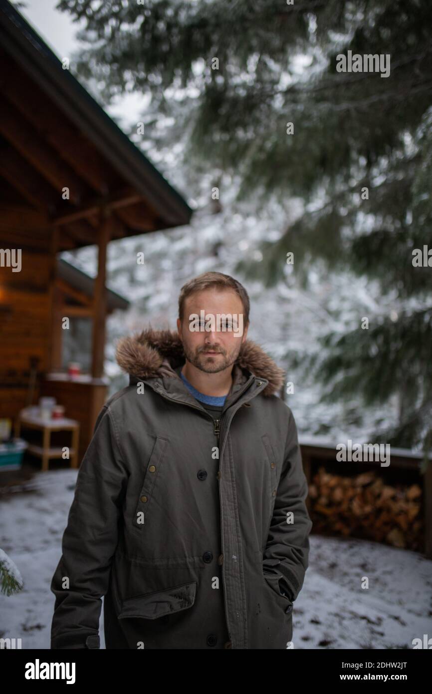 Handsome man standing with a cabin and snowy pines as background Stock ...