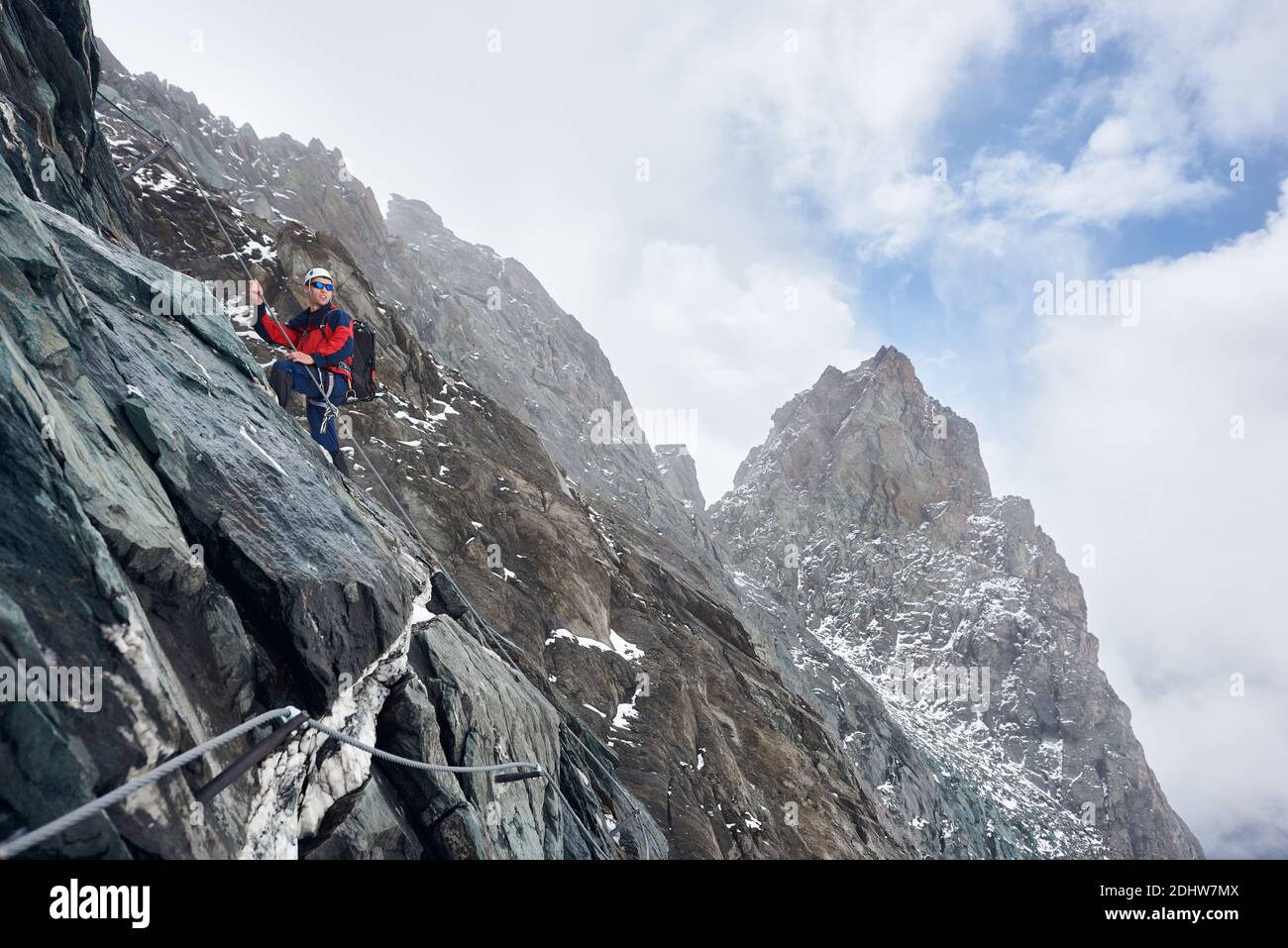 Male alpinist in sunglasses and safety helmet holding fixed rope while ...