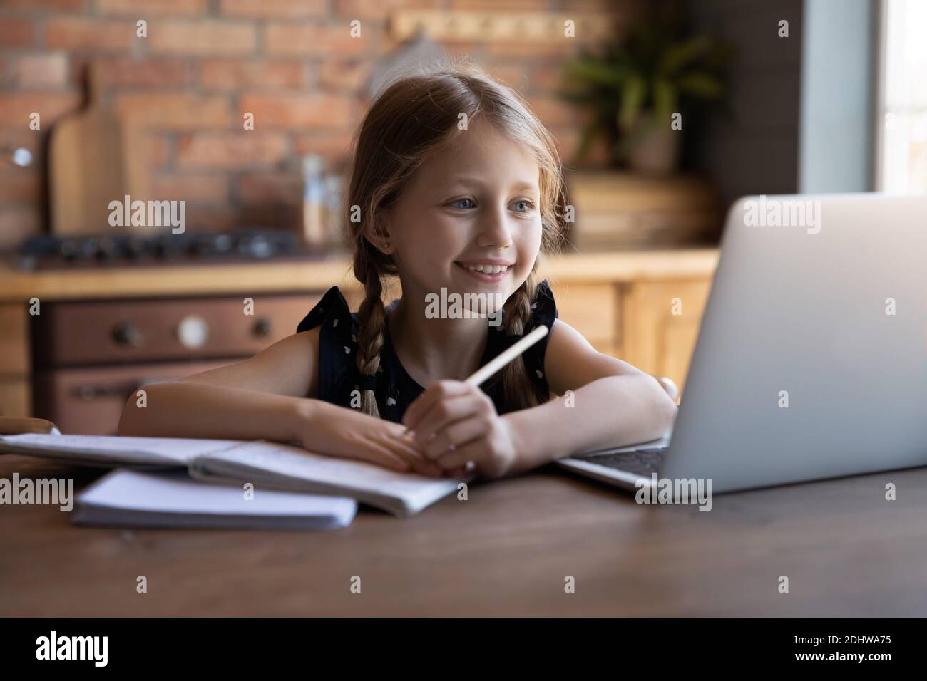 Smiling little girl watching online lesson, writing notes ...