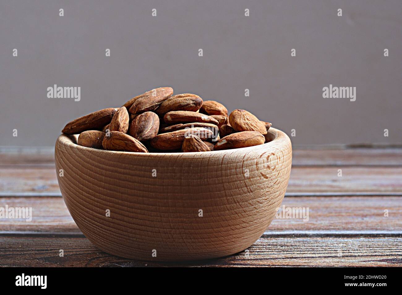 Wooden bowl full of unblanched almonds standing on wooden boards. Side ...