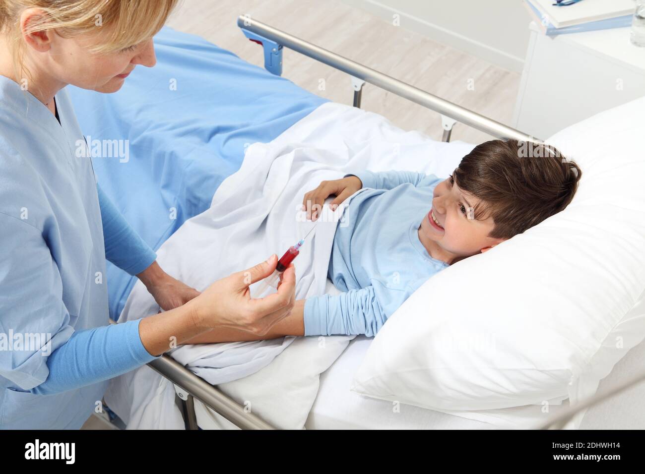nurse makes a blood test to the sick child in bed in the hospital room ...