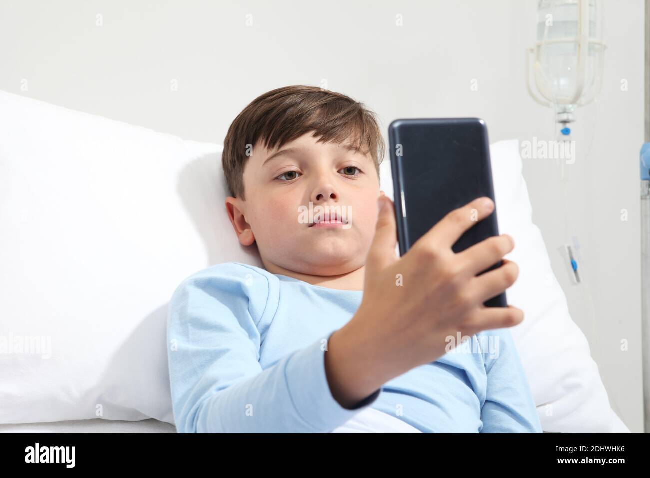 Portrait of child lying alone in bed in hospital room looking at ...