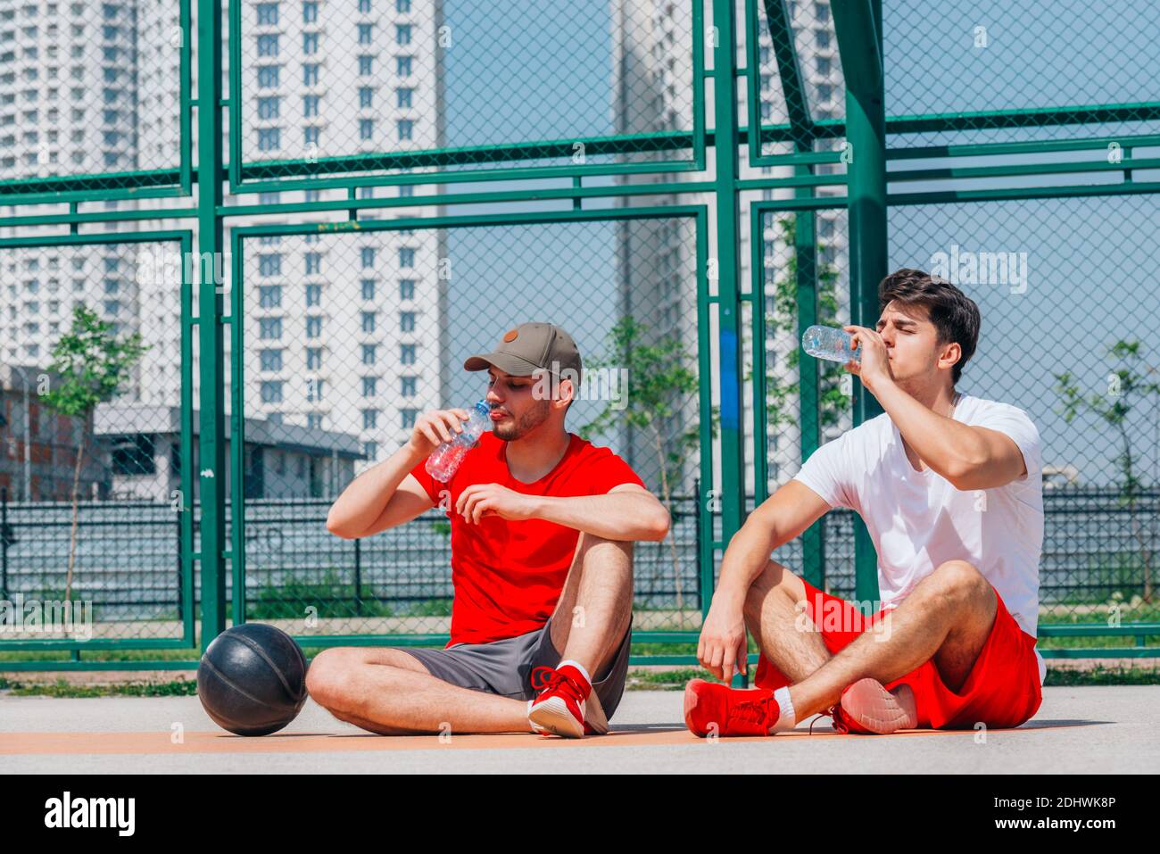 Two basketball players having some rest sitting on the court after an ...