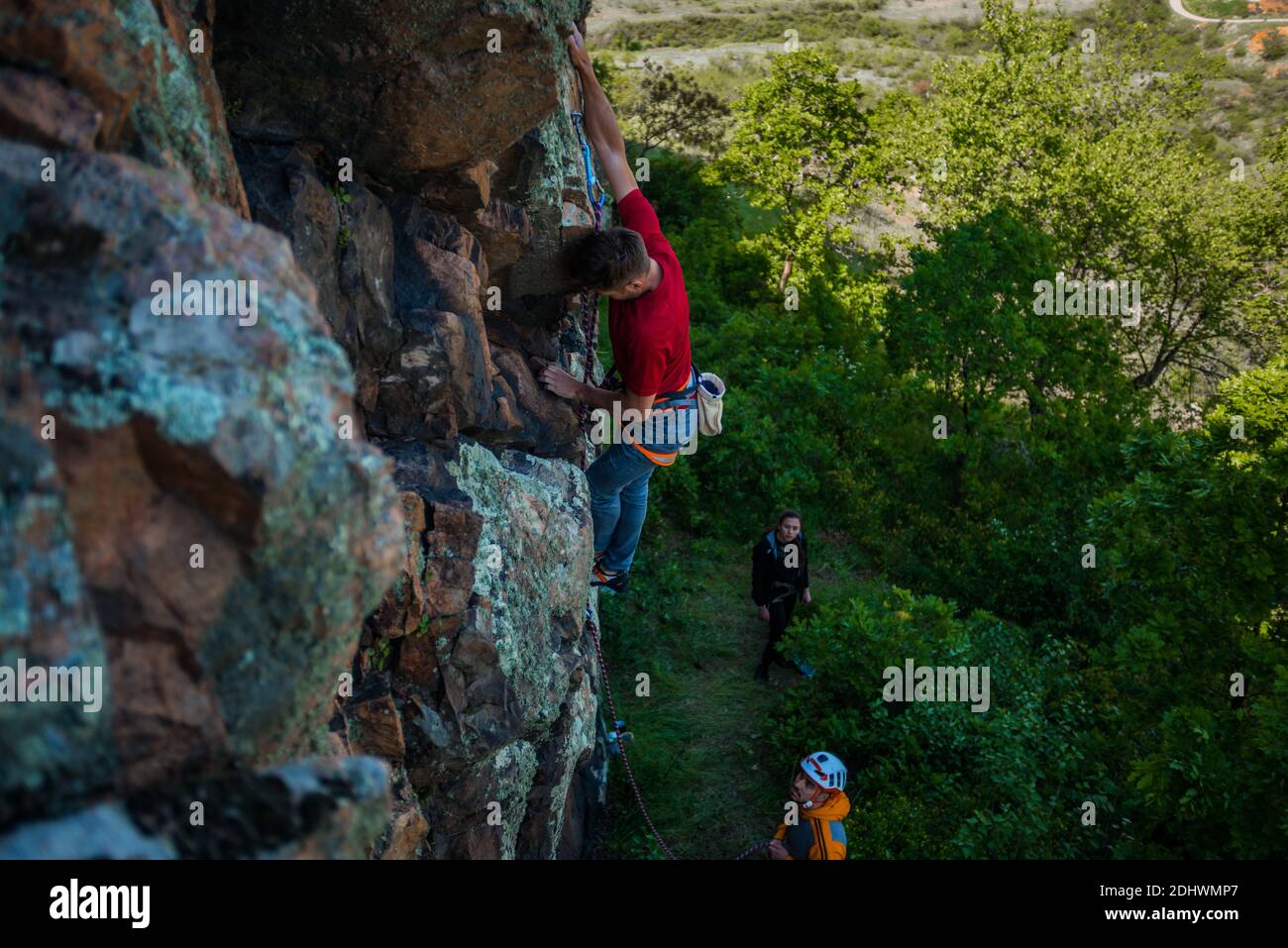 A man holding on to a piece of rock while he climbs up a steep cliff ...