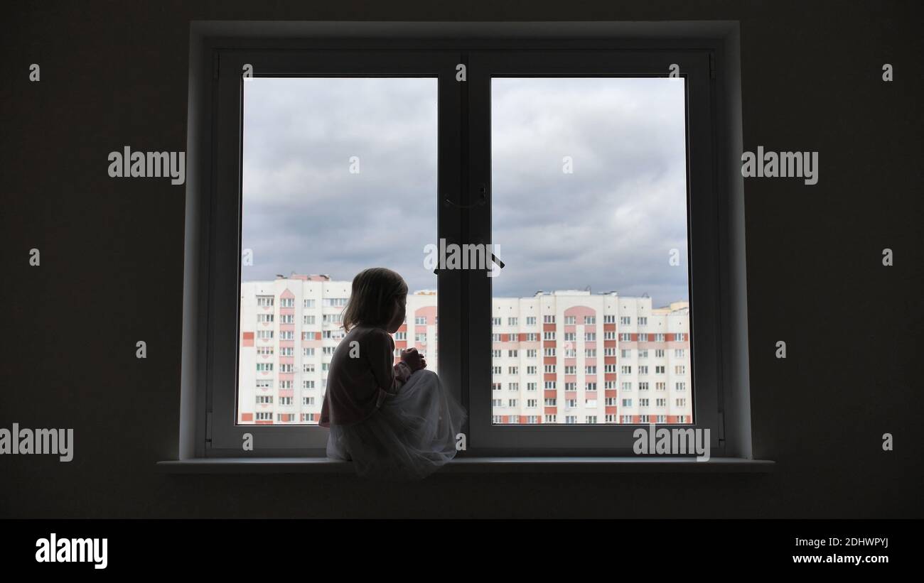 Lonely child girl sitting on the windowsill at the window in the ...