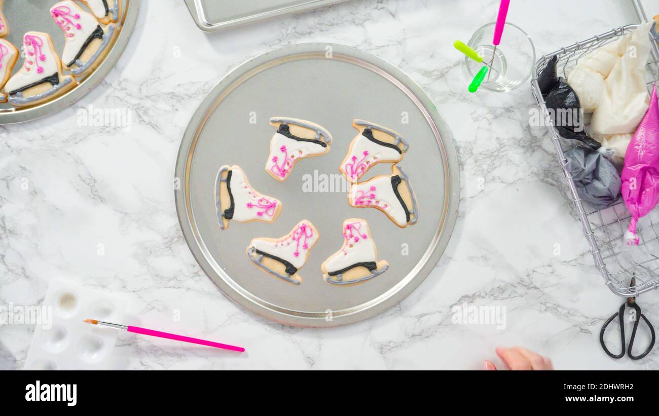 Flat lay. Brushing edible glitter on iced figure skate sugar cookies ...