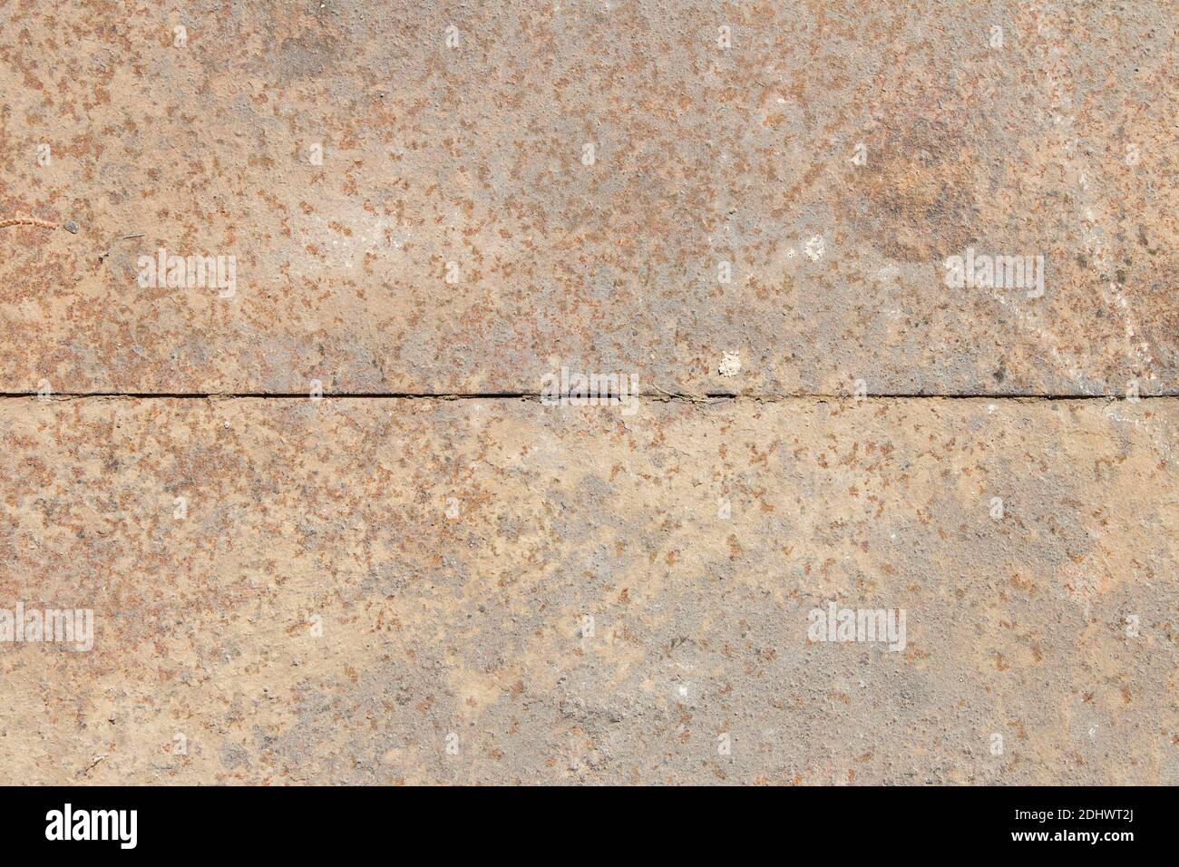A metal sheet covered in rust and sand is divided into two by a ...