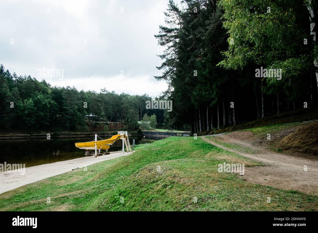 A yellow water slide next to a lake surrounded by a forest Stock Photo ...