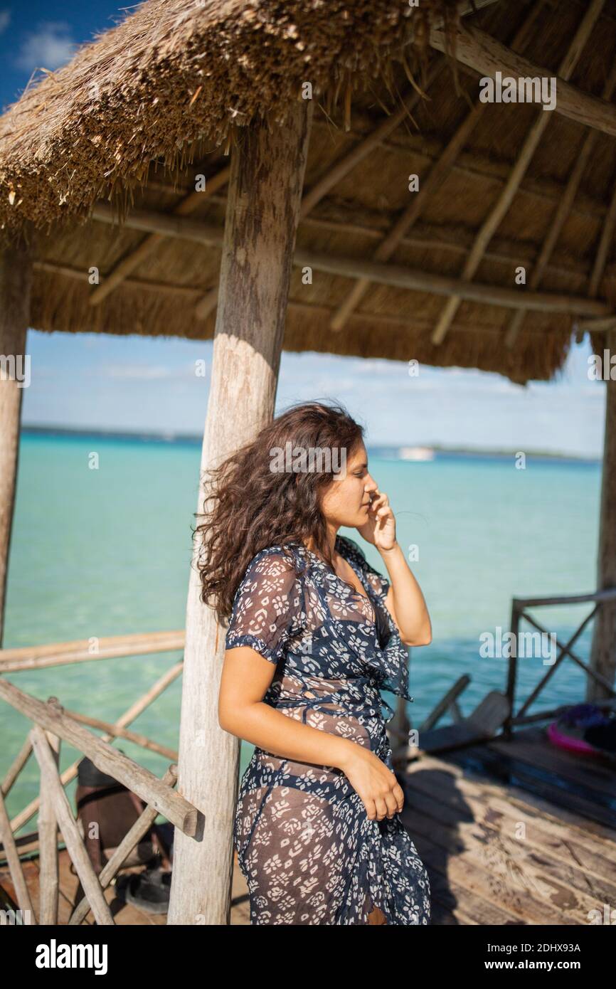 Beautiful woman leaning against the pole of a tiki hut Stock Photo - Alamy